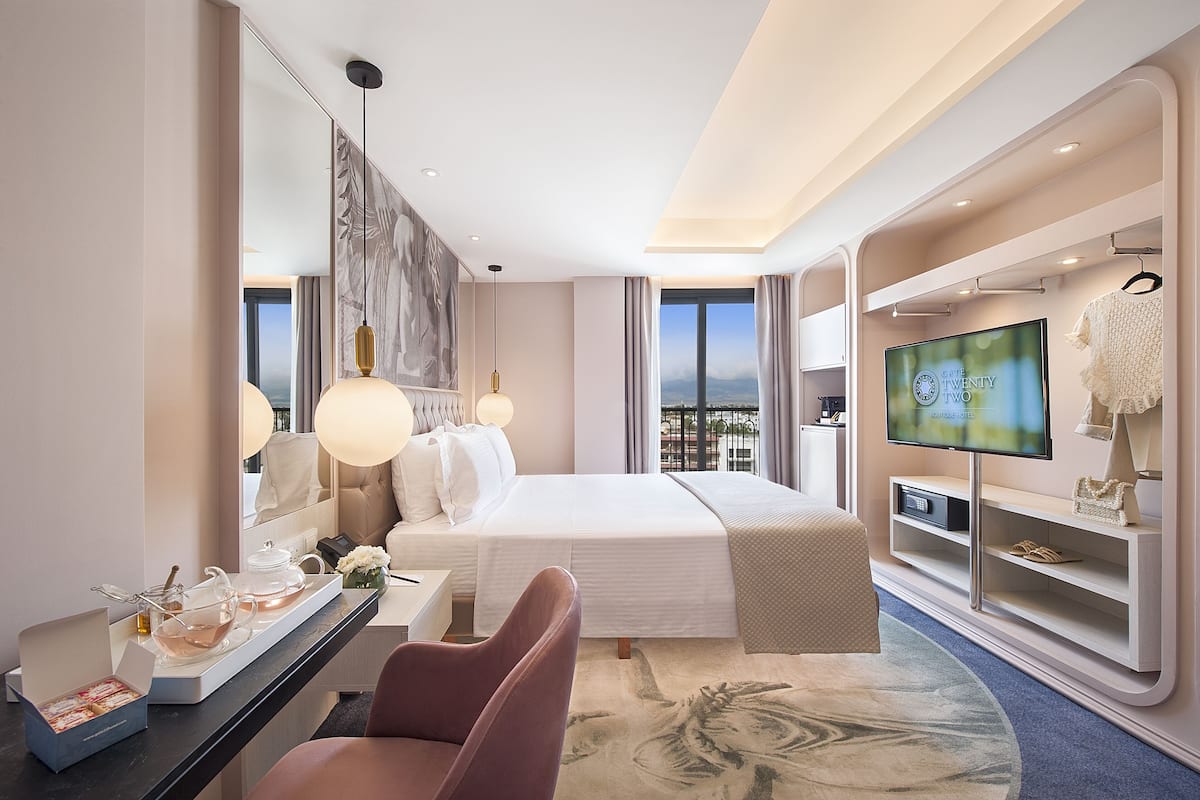 Quarto de hotel moderno com uma cama grande, uma TV, uma toucador com espelho e vista para a cidade.