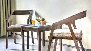 Uma área de refeições com duas cadeiras de madeira, uma mesa, uma tigela de frutas e dois copos de suco de laranja.