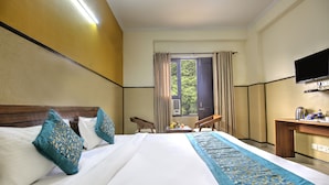 Quarto de hotel com uma cama grande, uma mesa, uma cadeira, uma televisão e uma janela com cortinas.