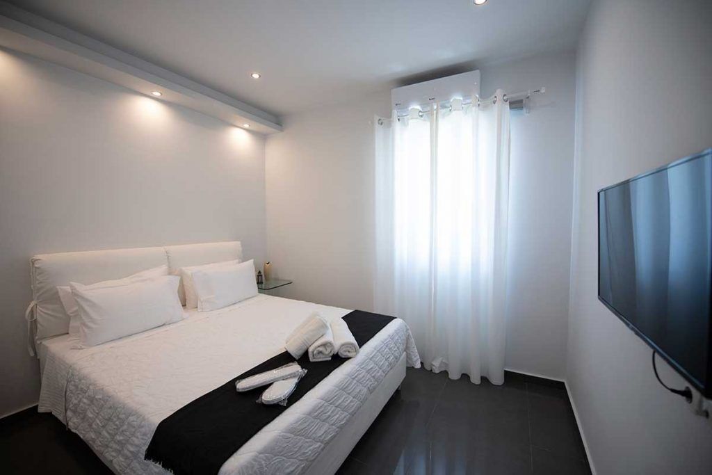 Quarto de hotel com uma cama grande, roupa de cama branca, televisão de tela plana e janela com cortinas.