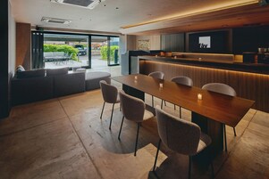 Um hall de hotel moderno com uma receção em madeira, uma televisão de ecrã plano grande e uma área de estar com sofás e cadeiras.