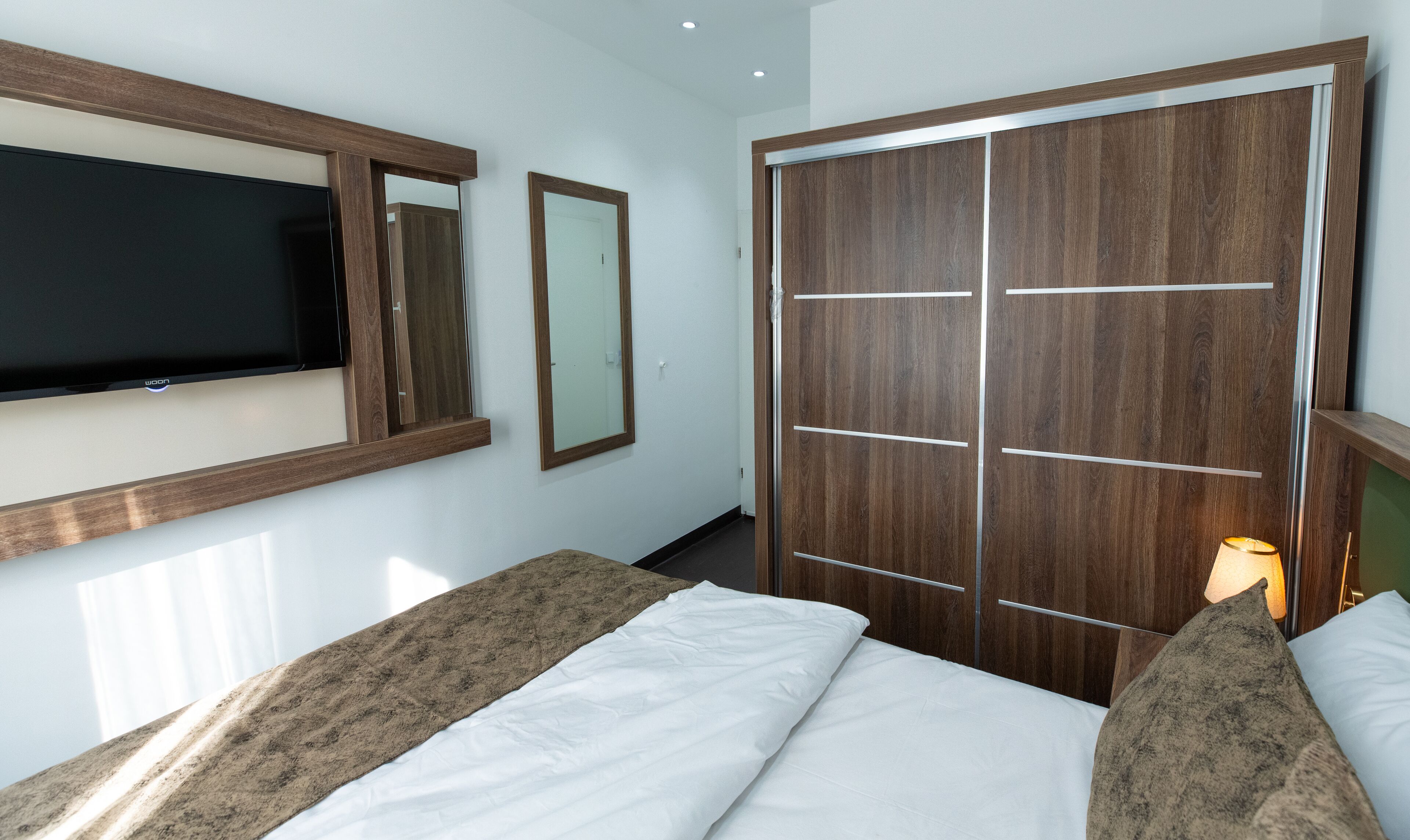 Quarto de hotel com cama, televisão, guarda-roupa e abajur.