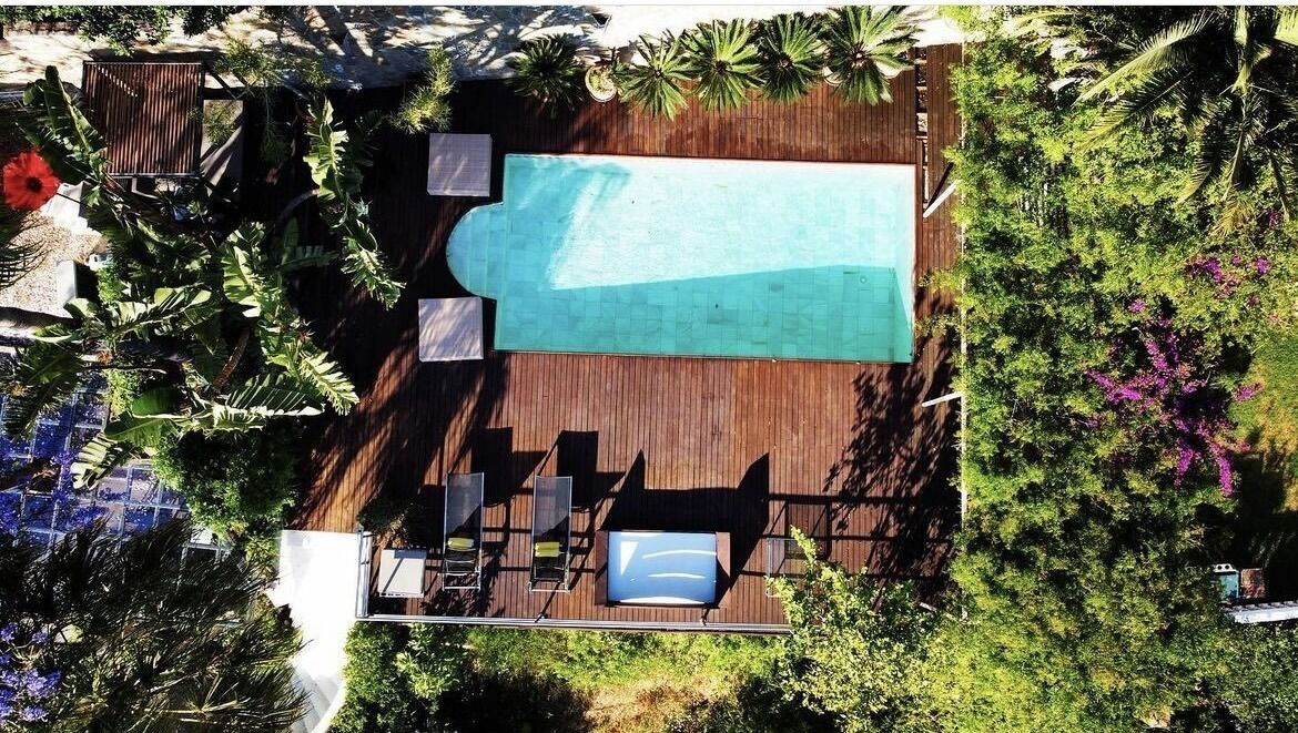 Vista aérea de uma área de piscina com deck de madeira, espreguiçadeiras e uma piscina pequena.