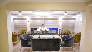 Uma sala de jantar com um lustre moderno, uma mesa com tampo de vidro e quatro cadeiras com pés dourados.