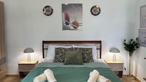Cama bem arrumada com colcha verde, duas luminárias de cabeceira e uma pintura abstrata pendurada na parede.