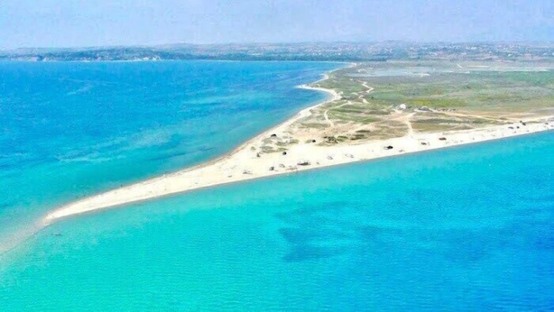 Vista aérea de uma área costeira com uma praia de areia e águas azul-claras.