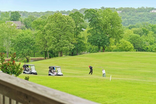 Um campo de golfe com um clube, um putting green e uma colina arborizada ao fundo.