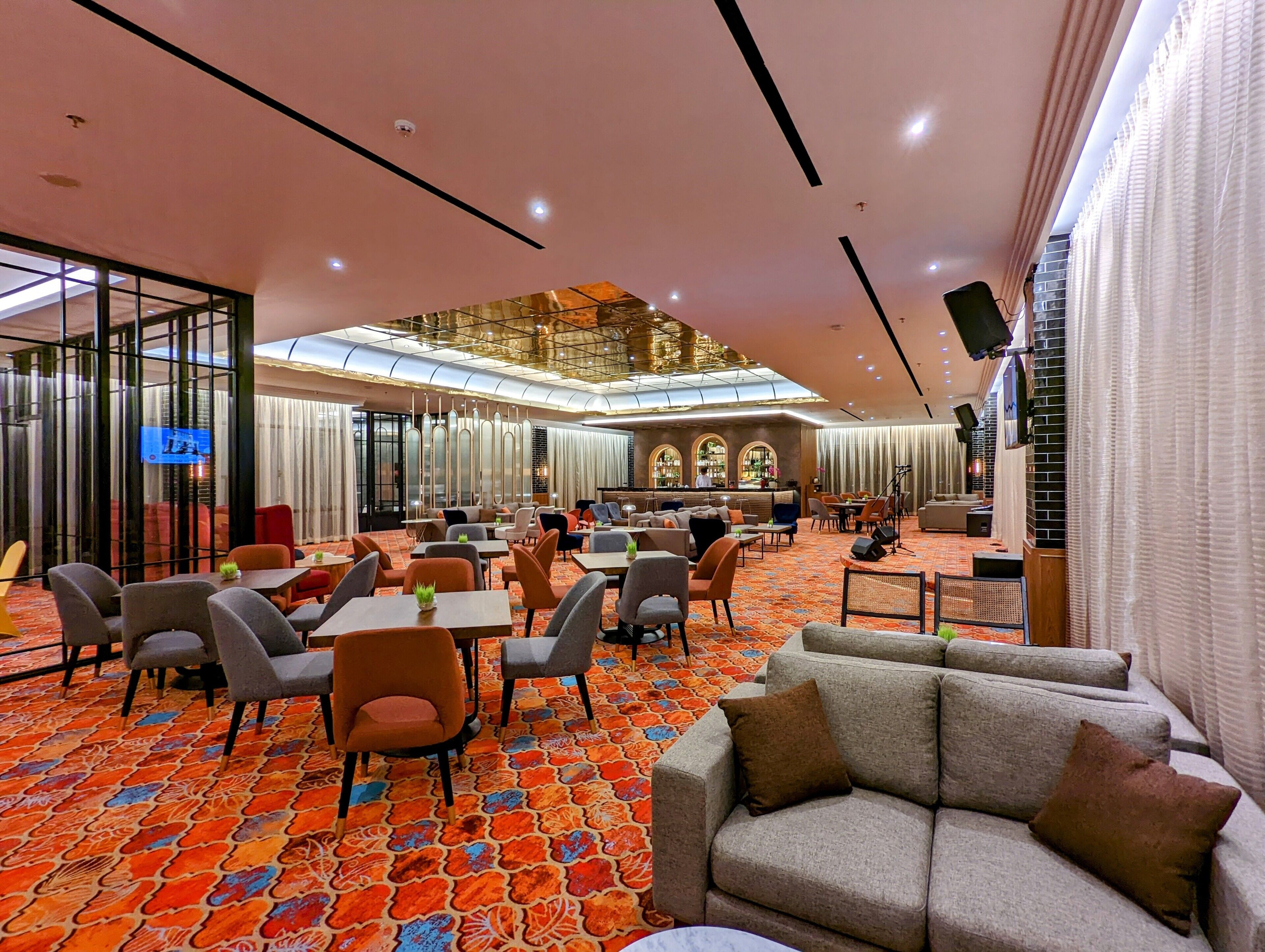 Um hall de hotel espaçoso com teto alto, área de bar central e espaço de estar com sofás e cadeiras.
