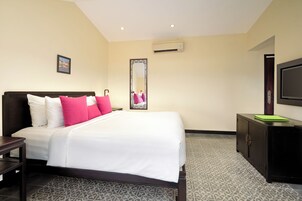 Quarto de hotel com uma cama grande, mesa de cabeceira, cômoda, espelho, aparelho de ar condicionado e televisão.