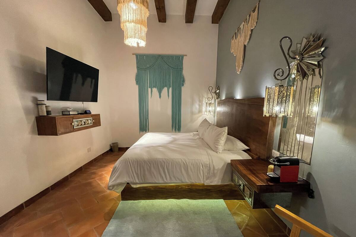 Um quarto com uma cama, televisão, cabeceira de madeira, espelho e uma pequena mesa.