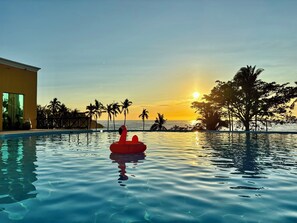 Piscina com boia inflável vermelha, palmeiras e vista para o pôr do sol.