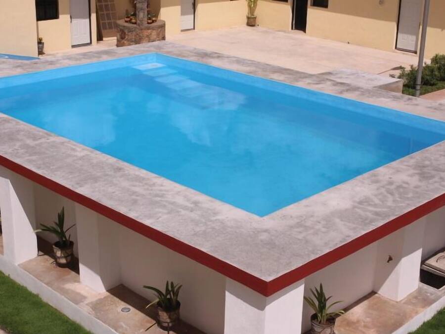 Uma piscina retangular com borda branca e vermelha, rodeada por um muro branco baixo e plantas em vasos.