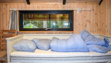 Quarto de cabana de madeira com uma cama, uma janela e vista para uma floresta.