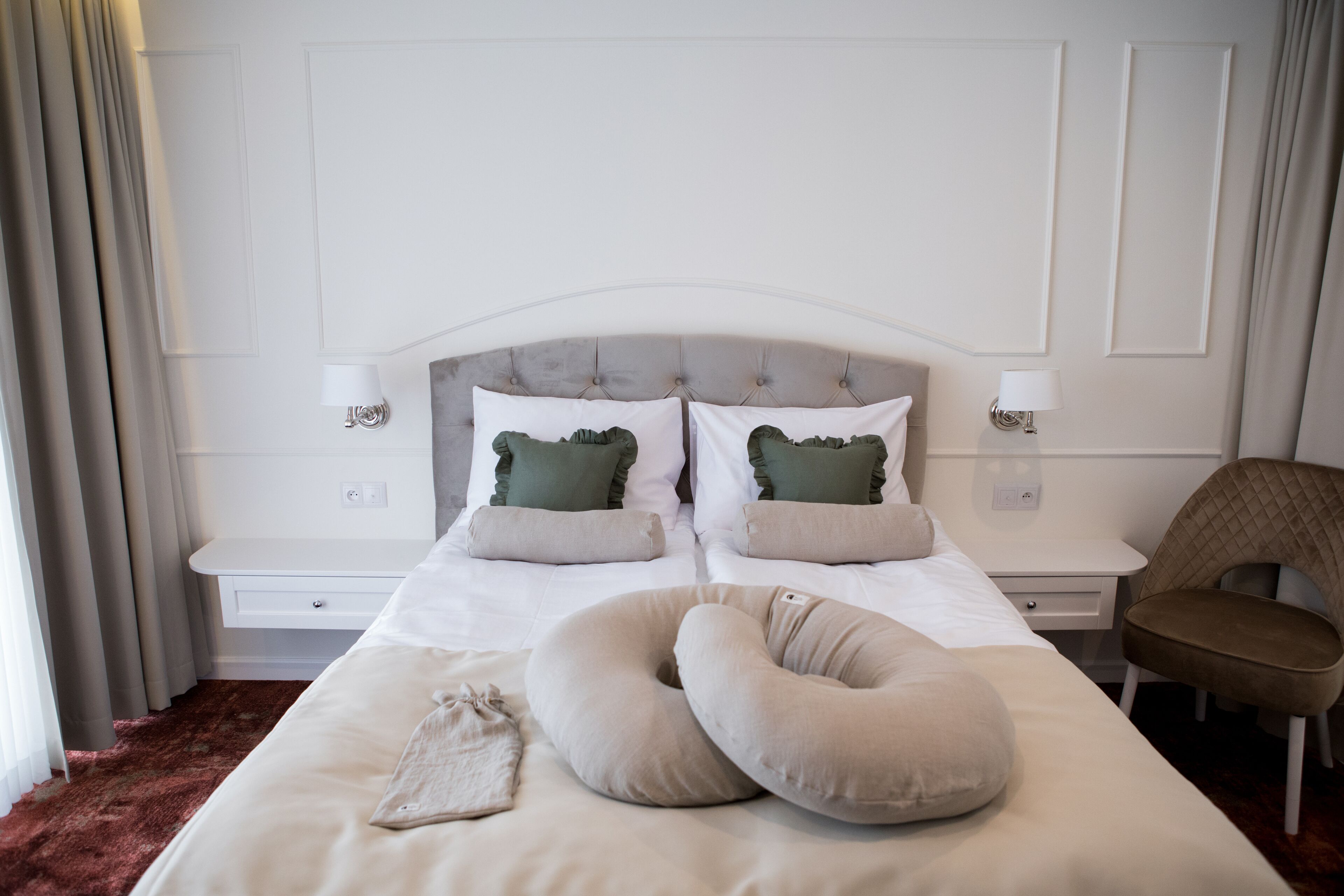 Quarto de hotel bem arrumado com uma cama grande, duas mesas de cabeceira com abajures, uma cadeira e um travesseiro decorativo.