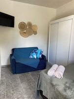 Quarto com sofá azul escuro, televisão de tela plana na parede e cama com toalha enrolada.