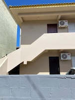 Um edifício com fachada bege, porta escura e dois aparelhos de ar condicionado fixados na parede.