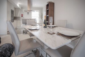 Uma área de jantar moderna com mesa de mármore, cadeiras brancas e uma garrafa de vinho.