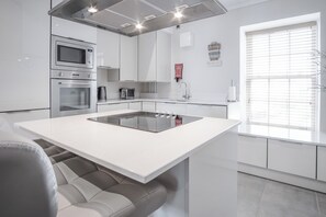 Cozinha moderna com ilha central, eletrodomésticos embutidos e janela com persianas.