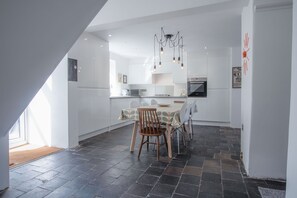 Uma cozinha moderna com armários brancos, uma mesa de jantar com cadeiras, um lustre e piso revestido de azulejos pretos.