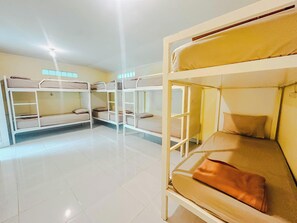 Quarto tipo dormitório com beliches, ventilador de teto e janela com persianas.
