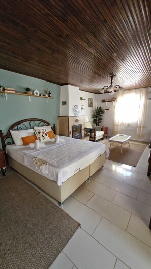 Quarto com cama, mesas de cabeceira, televisão, poltrona e uma pequena mesa.