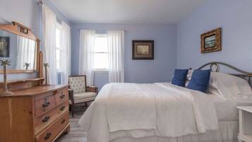 Um quarto com cama, cômoda, cadeira e quadros na parede.