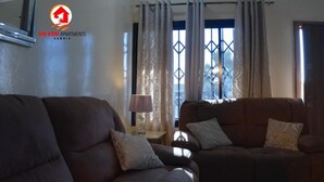 Uma sala de estar com dois sofás, uma luminária e uma janela com cortinas estampadas.
