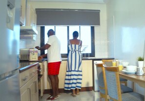 Uma cozinha com duas pessoas, uma mesa de jantar com cadeiras e uma janela.