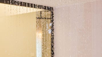 Chuveiro com recurso de água tipo chuva, um espelho e parede revestida com azulejos bege.