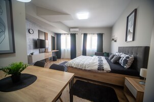 Quarto de hotel moderno com cama, mesa de cabeceira, televisão e área de refeições com mesa e cadeiras.