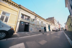 Vista da rua com edifícios, um carro estacionado e uma pessoa ao lado de um muro com grafite.