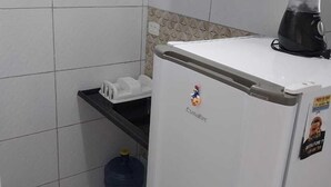 Uma cozinha compacta com armários brancos, micro-ondas, geladeira e liquidificador.