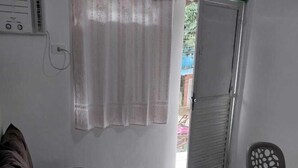 Quarto pequeno e limpo, com um sofá marrom, uma mesa com uma cadeira e uma porta que dá para uma área externa.