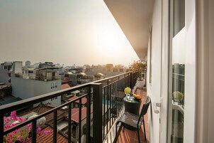 Varanda com mesa e cadeira, vista para a cidade ao pôr do sol.