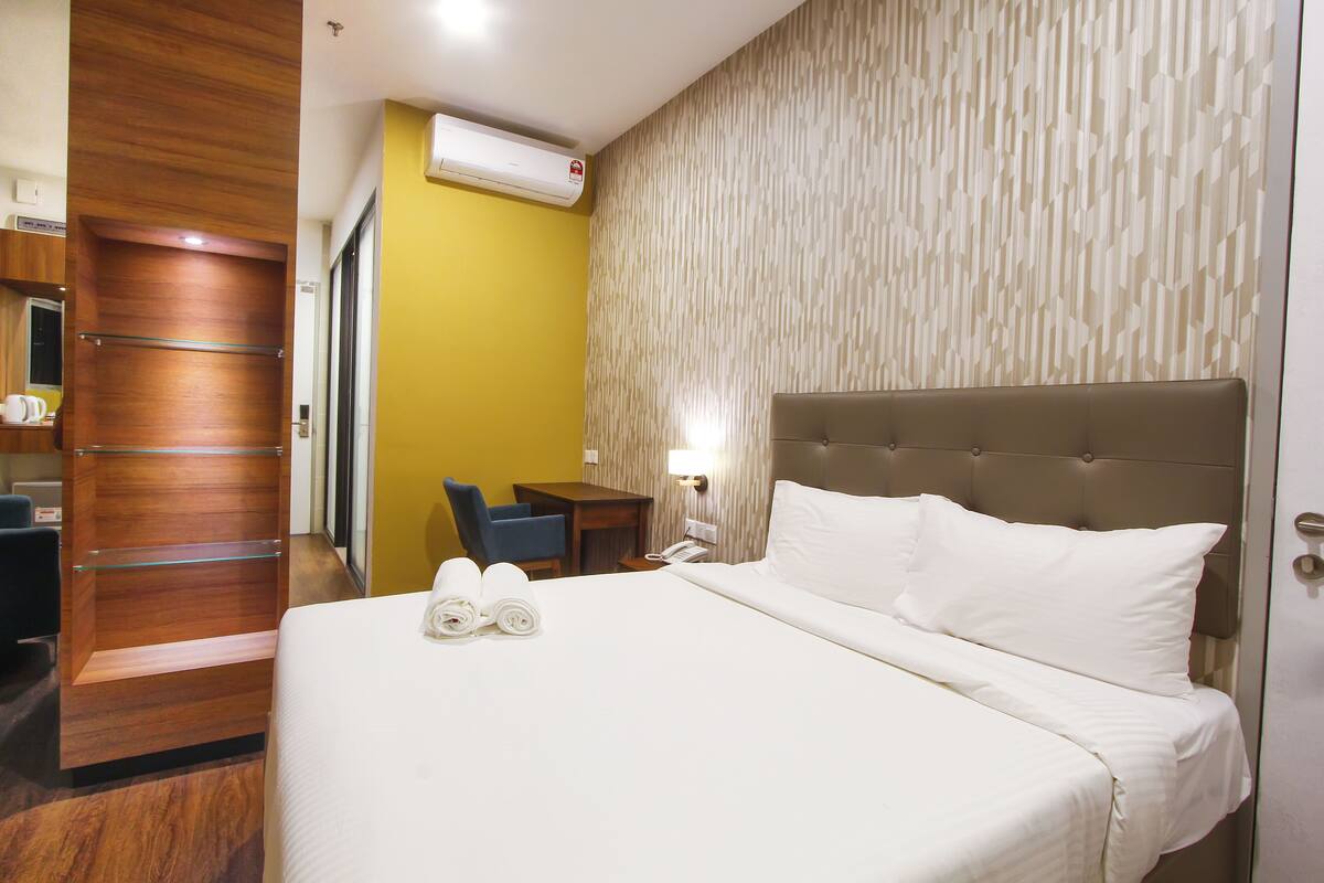 Quarto de hotel com cama, escrivaninha, cadeira e guarda-roupa.