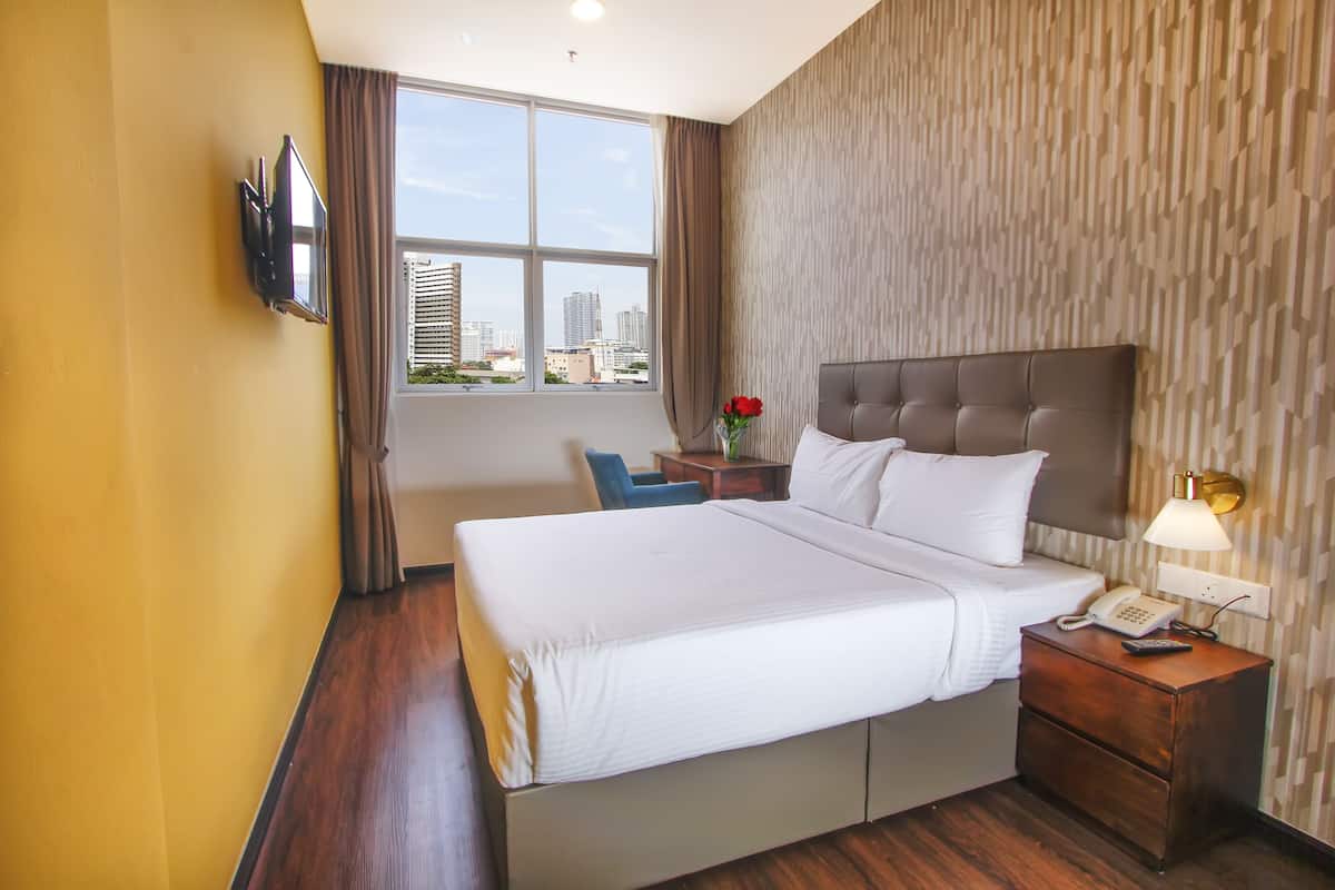 Quarto de hotel com uma cama grande, uma mesinha de cabeceira com abajur, telefone e vista da cidade pela janela.