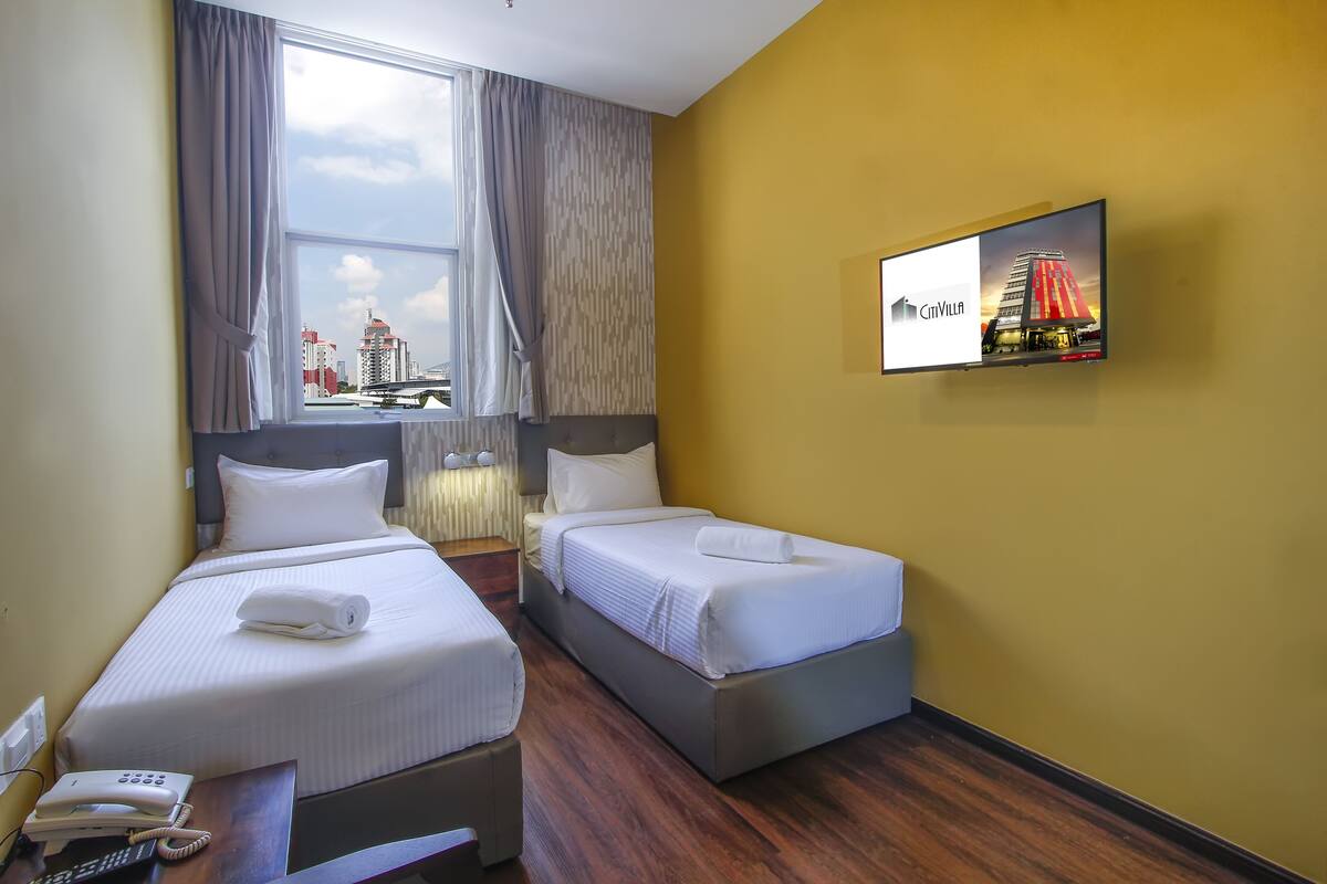 Quarto de hotel com duas camas, televisão, telefone e janela com cortinas.