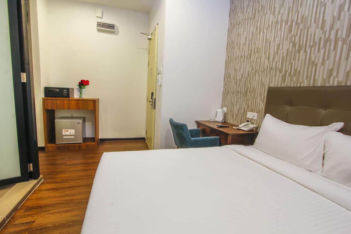 Quarto de hotel com uma cama grande, uma escrivaninha com telefone, uma cadeira e um pequeno armário com um vaso de flores.