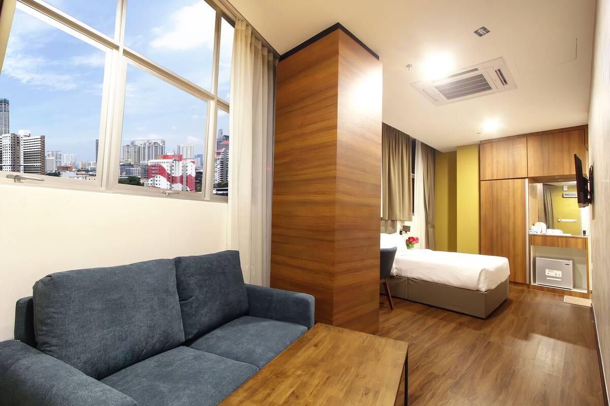 Quarto de hotel com sofá, cama, parede de destaque em madeira, televisão e vista para a cidade.