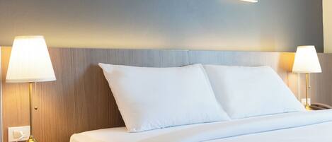 Quarto de hotel com cama, duas luminárias de cabeceira, mesa de apoio e luminária na parede.