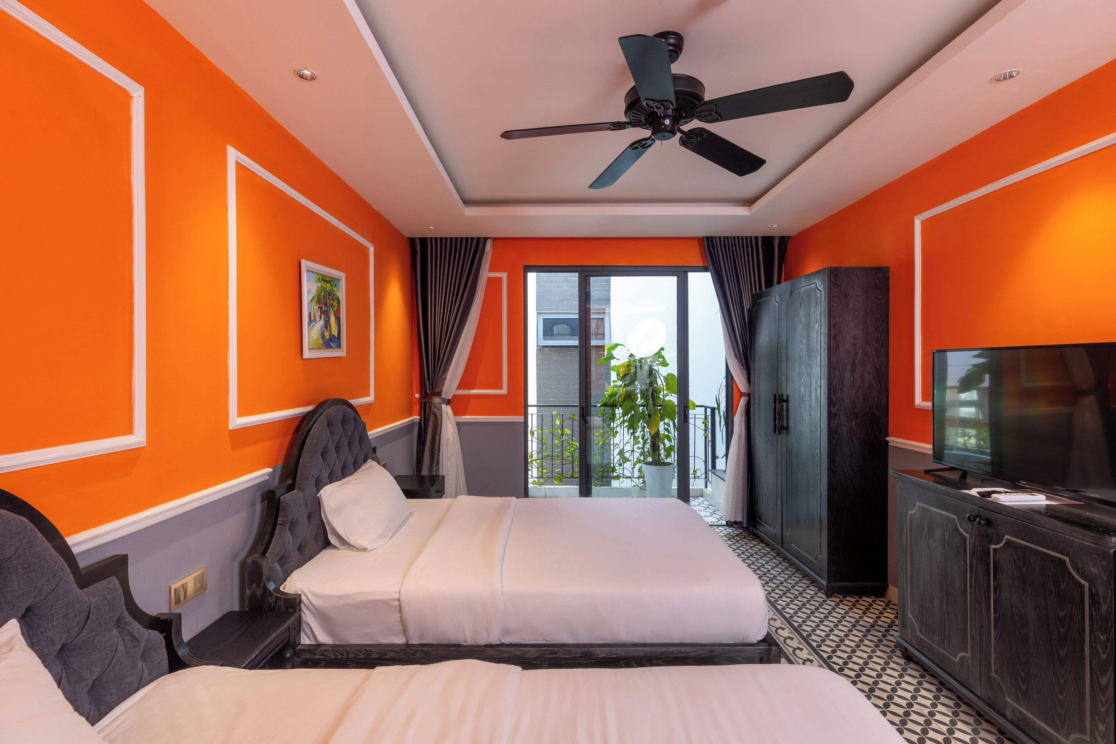 Quarto de hotel com duas camas, ventilador de teto, televisão, guarda-roupa e varanda com vista.