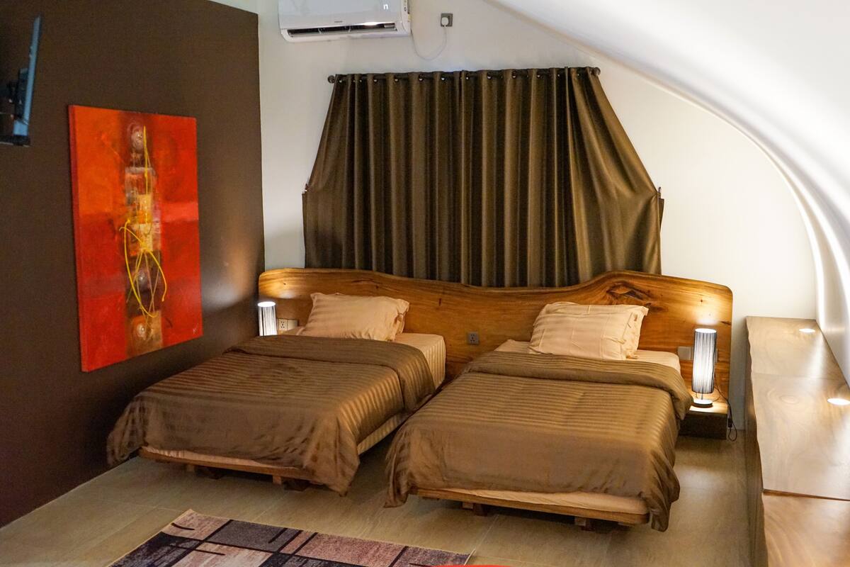 Quarto com duas camas, cabeceira de madeira, ar condicionado fixado na parede e um quadro.