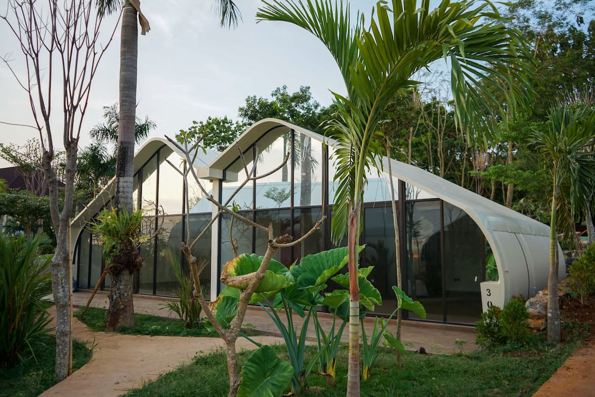Um edifício moderno com telhado curvo e amplas janelas de vidro, rodeado por vegetação tropical.