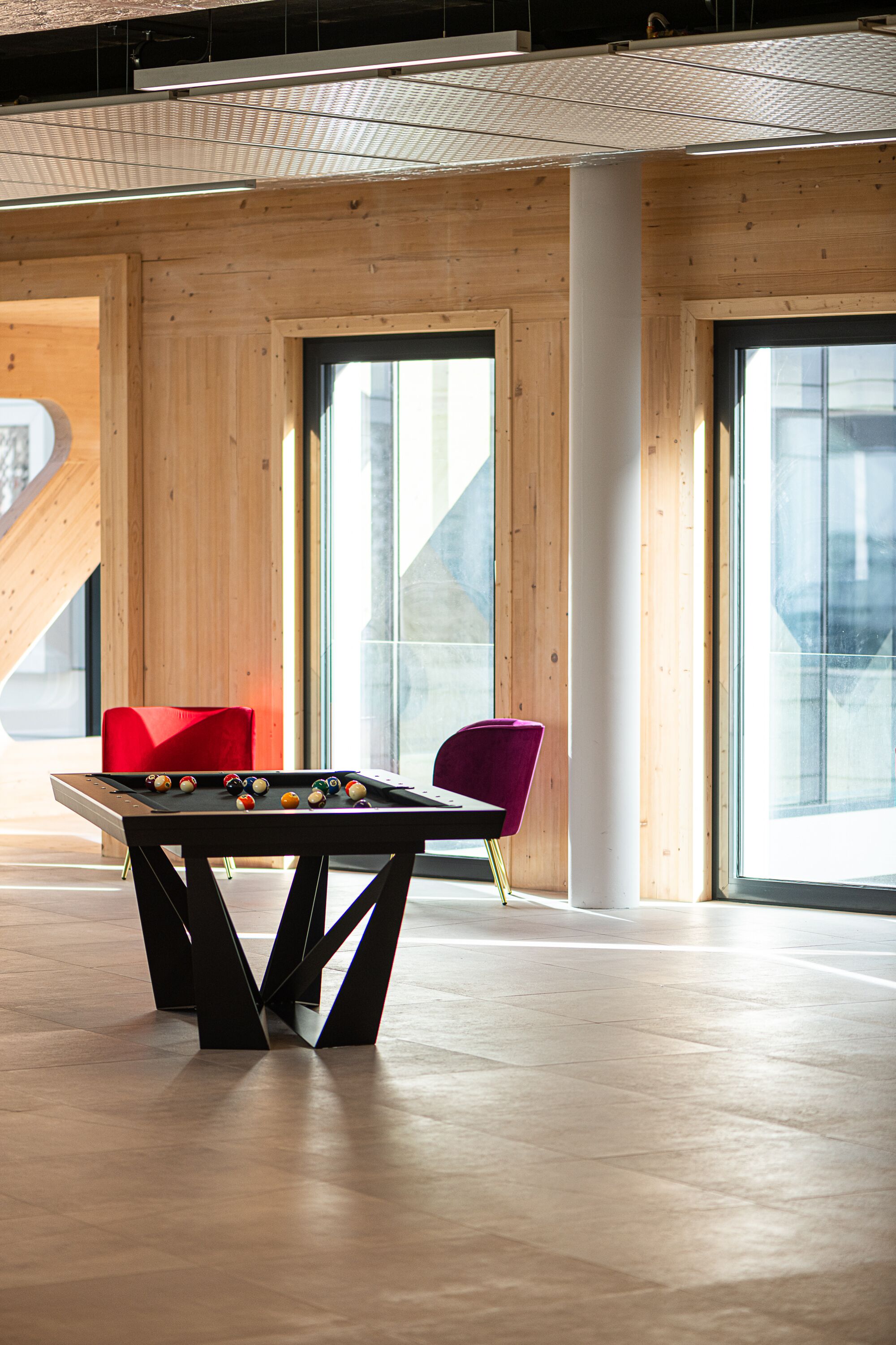 Uma mesa de bilhar com design moderno, rodeada por paredes de madeira e grandes janelas.