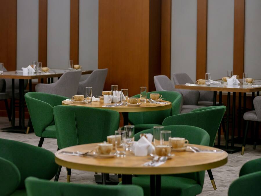Uma sala de jantar com mesas redondas, cadeiras estofadas em verde e um lustre moderno.