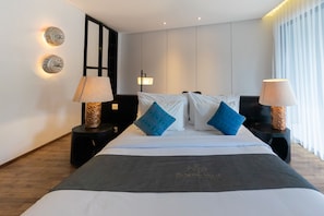 Quarto de hotel com uma cama grande, duas mesas de cabeceira com luminárias, um criado-mudo e um aplique na parede.