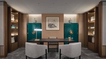 Uma sala de conferências com uma mesa de madeira escura, duas cadeiras estofadas cinzentas, armários verde-água com detalhes decorativos e uma obra de arte emoldurada na parede.