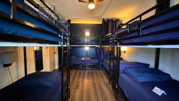 Quarto com beliche, ventilador de teto, piso de madeira e uma pequena mesa com um cartão.