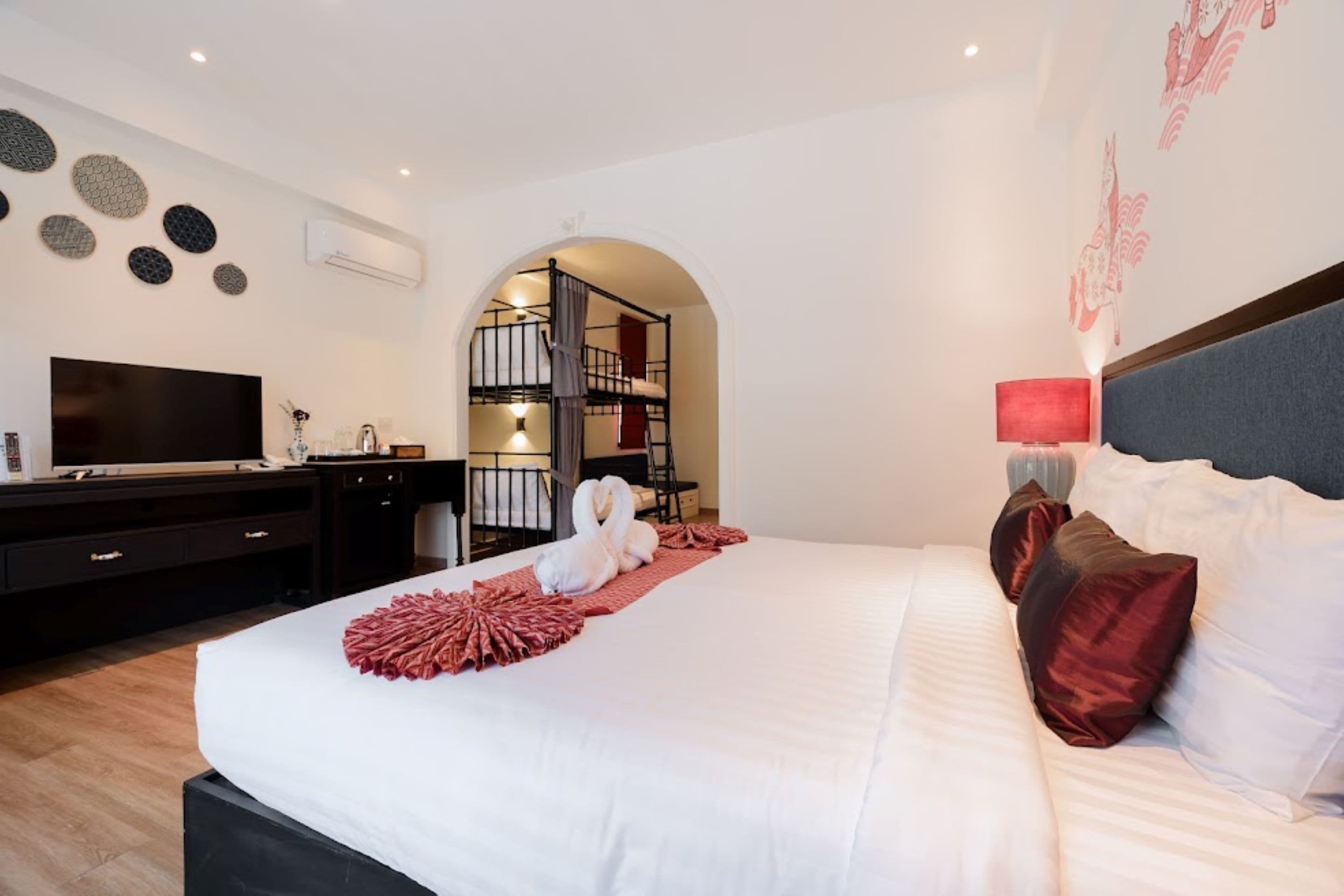 Quarto de hotel com uma cama grande, televisão, escrivaninha e escada que leva a um mezanino.