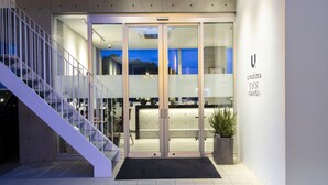 Entrada moderna de um hotel com porta de vidro, escadaria e placa indicativa de 'Urasima Inn Gangi'.